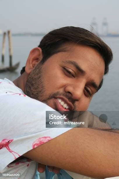 난간에 기대어 손에 머리를 기대고 자고 잘 생긴 인도 남자의 이미지 귀여운 힌두교 남자는 햇빛에 서 서 자려고 이빨을 보여주는 졸린 미소 짧은 손질 수염 눈을 닫고 해변