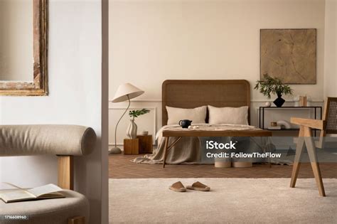 모형 포스터 프레임 세련된 침대 베이지 색 침구 등나무 안락 의자 밝은 양탄자 둥근 상자 슬리퍼 램프 및 개인 액세서리가있는 침실 인테리어의 아늑한 구성 가정 장식 템플렛