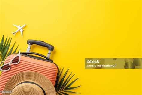 바람직한 여행 개념입니다 밀짚모자와 선글라스를 쓴 주황색 여행 가방과 야자수 잎과 비행기 모형이 있는 격리된 밝은 노란색 배경에 카피스페이스가 있는 위 보기 사진 여행
