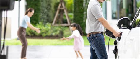 흐릿한 가족 배경으로 Ev 자동차를 충전하는 진보적인 남자의 초점 이미지 프리미엄 사진