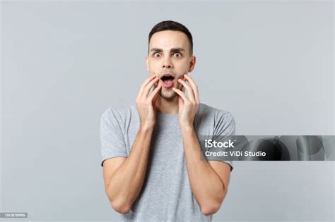 깜짝 놀란 젊은 남자의 초상화 입을 열어 스튜디오에서 회색 배경에 고립 된 얼굴에 손을 넣어 사람들은 진심으로 감정 라이프 스타일 개념입니다 복사 공간을 모의 합니다 T