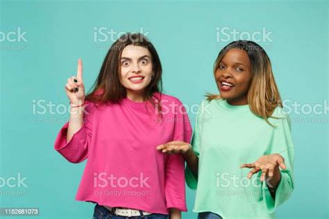 두 젊은 여자 친구 파란색 청록색 벽 배경 스튜디오 초상화에 고립 된 포즈를 서 있는 분홍색 녹색 옷에 유럽과 아프리카계 미국인 사람들 라이프 스타일 개념입니다 복사 공간을