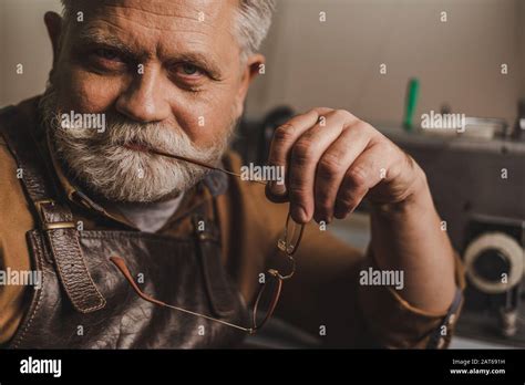 Positive Senior Shoemaker Smiling At Camera While Holding Glasses