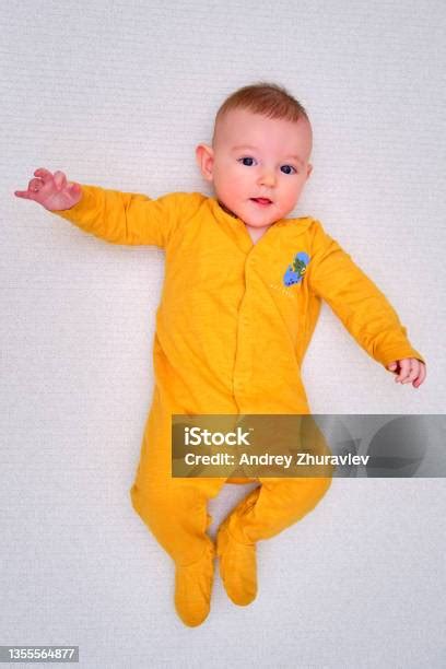 노란 잠옷을 입은 놀이 매트위에 누워 있는 행복한 유아 아기 상단 보기 흰색 바닥에 전체 길이 웃는 유아 복사 공간 누워있기에