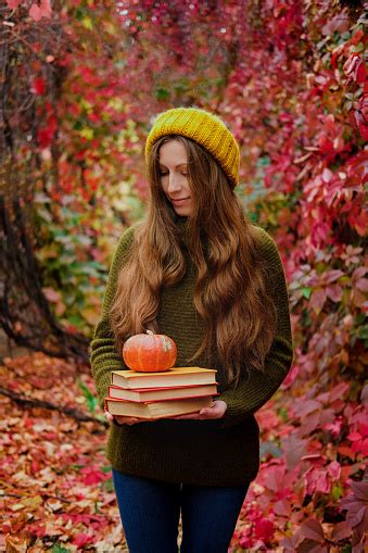 겨자 노란색 니트 모자와 습지 녹색 양모 스웨터에 소녀는 가을에 화려한 아이비 사이에 세 개의 빈티지 종이 책과 작은 호박의 스택을 들고 10월에 대한 스톡 사진 및 기타