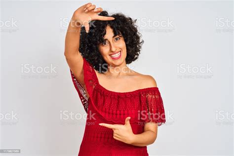 행복한 얼굴로 손과 손가락으로 프레임을 만드는 고립 된 흰색 배경 위에 서있는 빨간 드레스를 입은 곱슬 머리를 가진 젊은 아랍 여성 창의력과 사진 개념 개념에 대한 스톡