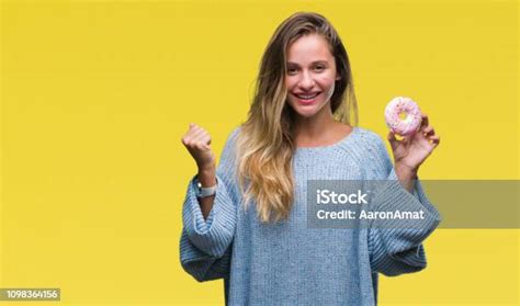 젊은 아름 다운 금발의 여 자가 자랑 비명과 축 하 하는 승리와 성공을 매우 흥분된 하 고 격리 된 배경 위에 달콤한 도넛을 먹고 환호 하는 감정 감정에 대한 스톡 사진 및