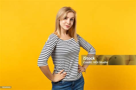 노란 주황색 벽 배경에 고립 된 허리에 팔을 안고 서 카메라를 찾고 줄무늬 옷에 젊은 여자를 웃는 사람들은 진심으로 감정 라이프 스타일 개념입니다 복사 공간을 모의 합니다