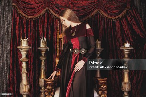 중세 여왕은 실내에서 성곽 방 내부에서 포즈를 취하는 역사적인 이미지에서 포즈를 취한다 요새의 골동품 황금 왕좌에 서 있는 옛 스타일의 슬픈 아가씨 극장 공연의 개념입니다