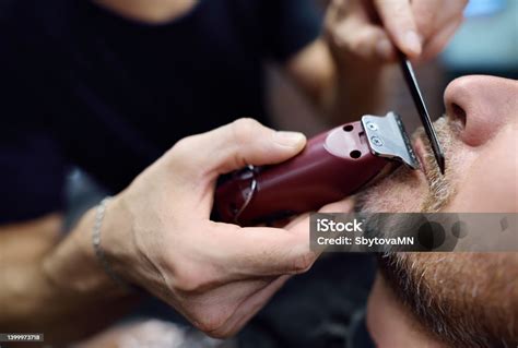 이발소 주인은 살롱에서 잘 생긴 성숙한 수염을 가진 남자를 면도하고 있습니다 이발소에있는 사람을위한 헤어 스타일을 만드는 헤어