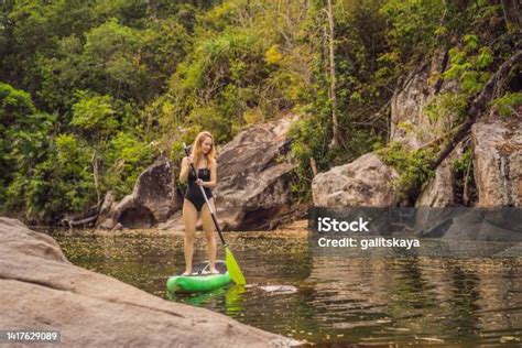 Sup 스탠드 업 패들 보드 여성 패들 탑승 호수에 앉아 푸른 물 위의 패들 보드에 행복하게 서 있습니다 패들 보드에서 젊은 여성의 액션 샷 30 34세에 대한 스톡 사진