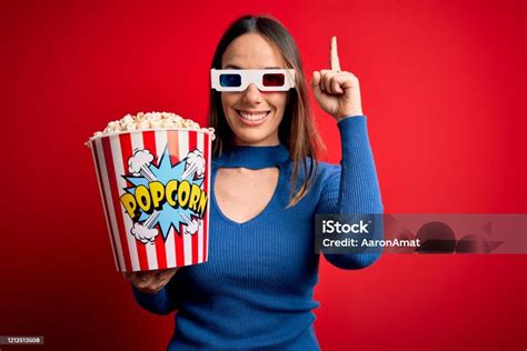 3d 안경을 쓰고 성공적인 아이디어로 손가락을 가리키는 영화관에서 영화를 보는 팝콘 팩을 먹는 젊은 금발 여성 종료하고 행복 넘버 원 3차원 형태에 대한 스톡 사진 및 기타