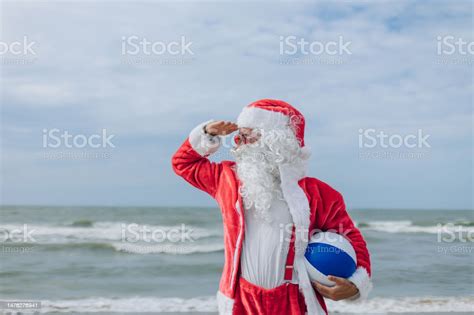 그의 팔 아래에 비치 볼을 가진 산타 클로스는 수평선을 본다 배경의 해변 12월에 대한 스톡 사진 및 기타 이미지 12월 8월 개념 Istock