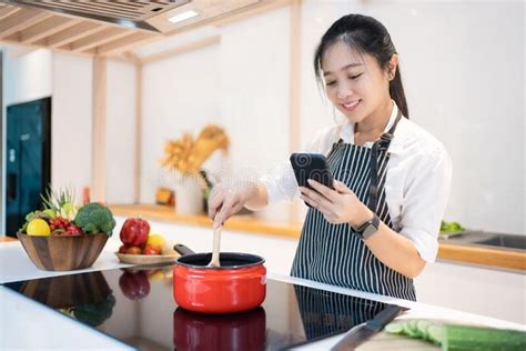Beautiful Asian Woman Cooking In The Kitchen She Is Looking At Recipes