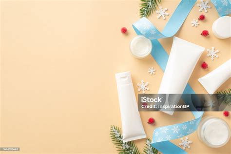 겨울 시즌 스킨케어 제품 개념 흰색 화장품 병의 상위 뷰 사진 서리 블루 곱슬 리본 마가목 열매와 눈송이 복사 공간이 있는 격리된 베이지색 배경에 12월에 대한 스톡 사진