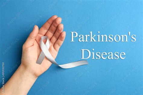 Female Hand With Silver Ribbon And Text Parkinson S Disease On Blue Background Stock Photo