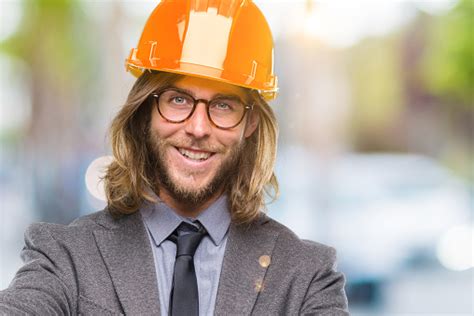 포옹에 대 한 두 팔을 벌려 웃 고는 카메라를 보고 하는 고립 된 배경 위에 안전 헬멧을 쓰고 긴 머리를 가진 젊은 잘생긴 Architec 남자 명랑 식 수용 행복입니다