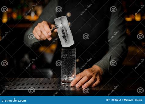 Bartender Putting A Big Ice Cube Into An Empty Glass On A Bar Co Stock