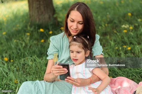 백인 어머니와 딸 아이는 여름날 공원에서 스마트 폰을 사용합니다 엄마와 아이는 화상 통화로 이야기하고 함께 자화상 사진을 찍습니다 여름 기술 소셜 미디어 가족 개념 아이에