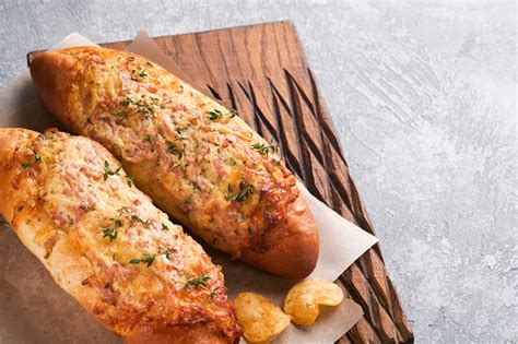 바게트 보트 양피지에 햄 베이컨 야채 및 치즈가 들어간 바게트 빵에 뜨거운 구운 샌드위치와 회색 콘크리트 배경에 나무 스탠드가 있습니다 상단 보기 공간을 복사합니다 가공육에