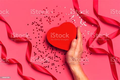 발렌타인 데이 컨셉 빨간 하트 모양의 선물 상자를 들고 있는 남자의 손 분홍색 배경 상단 뷰 플랫 레이에 색종이 사랑 생일 선물 어머니의 날 3 월 8 일 휴일 배경의