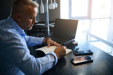 성숙한 사업가가 노트북에 쓰고 프로젝트를 계획하고 일기로 메모를 하고 세련된 인테리어가 있는 집에서 노트북 모니터 앞에 앉아 있는 모습 40 49세에 대한 스톡 사진 및