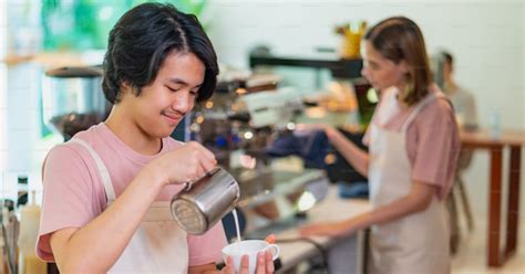 아시아 남자 바리스타가 커피 컵에 라떼 아트 커피를 만드는 거품 우유를 붓고 있다 남성 커피숍 파트타임 직원이 커피 메이커에서