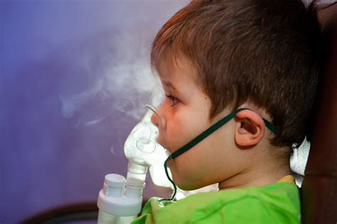 마스크를 쓴 어린 소년은 집에서 분무기로 호흡기를 치료합니다 아기는 그의 입에 분무기와 함께 앉아 흡입기 기관지염의 치료 물리치료에 대한 스톡 사진 및 기타 이미지 Istock