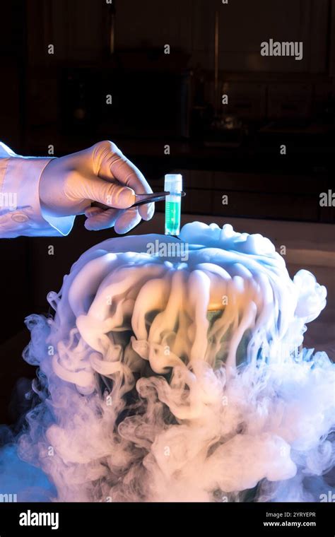 Gloved Hand Using Tweezers To Place Green Test Tube In Liquid Nitrogen Creating A Smoky Effect