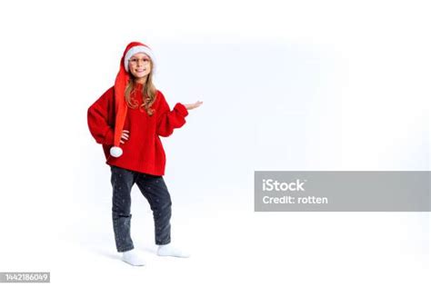 고립된 배경 위에 크리스마스 모자를 쓴 젊은 아름다운 소녀는 쾌활한 발표를 하고 카메라를 바라보는 손바닥으로 가리키고 있다 가리키기에 대한 스톡 사진 및 기타 이미지