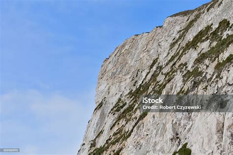 A Craggy Cliff Face Stretches Upwards Against A Clear Blue Sky Stock