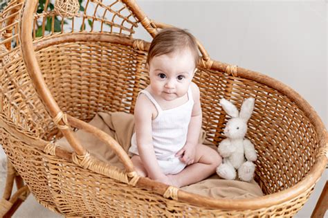 부드러운 장난감 토끼가 미소를 짓는 흰색 바디 수트를 입은 밝은 침실 보육원의 고리 버들 세공 침대 요람에있는 작은 소녀 6