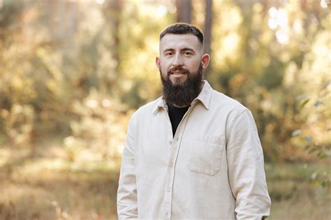 흰색 캐주얼 재킷을 입은 젊은 웃는 수염 난 남자의 초상화는 시골이나 공원의 가을 자연 배경에서 카메라를 봅니다 스타일의 개념 신선한 공기 속에서 걷고 자연과의 단결 30