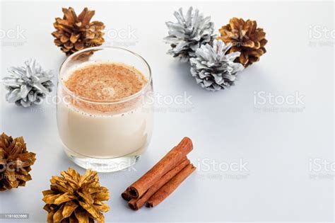 계란 알코올 강판 육두구와 계피 클로즈업 복사 공간을 가진 전통적인 크리스마스 칵테일 Eggnog 베이지 색 장식 불타는 등불과 소나무 콘이있는 회색 테이블에 달콤한 전통