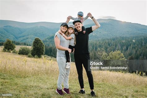 들판에서 함께 시간을 보내는 행복한 젊은 가족의 초상화 엄마 아빠는 아기 아들과 딸을 안고 산의 풀밭에 서 있다 가족 휴가의 개념입니다 어머니 아버지는 가을날에 아이들을