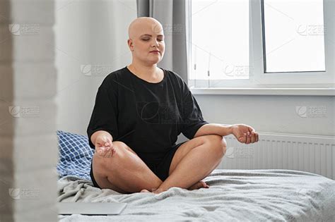 没有头发的快乐女孩坐在床上莲花的姿势