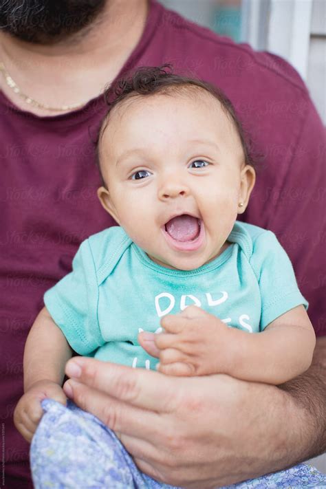 A Baby Smiling Happily As She Is Held By Her Father By Stocksy