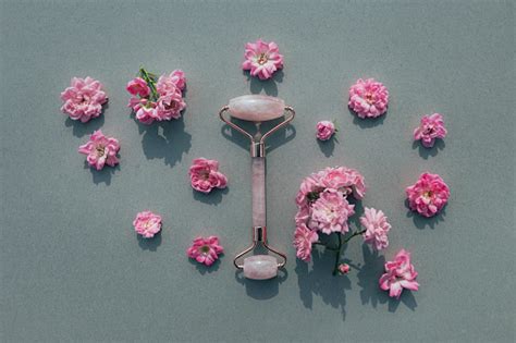 홈 스파를위한 얼굴 마사지 도구 장미 새싹이있는 회색 파스텔 배경에 장미 석영으로 만든 얼굴 롤러 자연 치료 개념 상단 보기