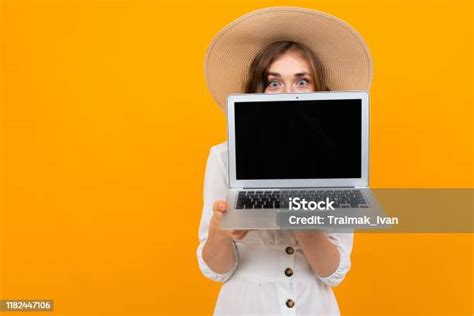 모자를 쓴 쾌활한 갈색 머리의 여성이 주황색 배경의 초상화와 함께 가슴 높이에서 노트북을 들고 있습니다 개념에 대한 스톡 사진 및 기타 이미지 Istock