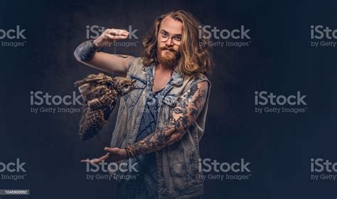 긴 무성 한 머리와 전체 수염 Tattoed 레드 Hipster 남자의 T셔츠를 입고 자 켓 스튜디오에서 올빼미의 허수 아비를 유지를 하 고 어두운 배경에 고립 개성 개념에