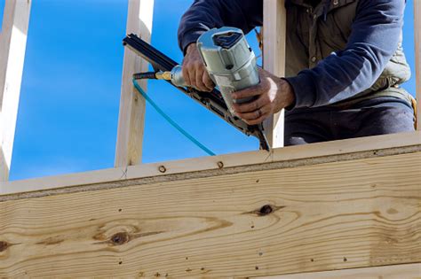 이 경우 건축업자는 주택 개발에서 건설을 위해 나무 빔을 못 박을 때 에어 해머를 사용합니다 목재 재료에 대한 스톡 사진 및 기타 이미지 Istock