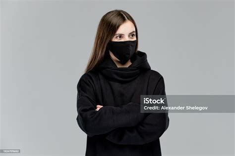 회색 배경에 스튜디오에서 검은 얼굴 마스크와 매력적인 여성의 초상화를 닫습니다 복사 공간이 있는 개념입니다 어린 소녀 착용 검정 의류 A 어두운 후드 25 29세에 대한