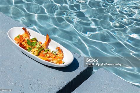 야채 Tabouleh와 향신료를 곁들인 튀김 새우는 타원형 세라믹 접시에 놓여 있습니다 접시는 수영장 근처의 콘크리트 스탠드에 서 있습니다 근처에는 라벤더 덤불이 있습니다