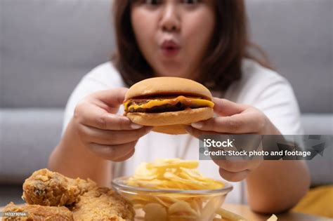 버거에서 선택적 초점 젊은 통통한 아시아 여성들이 거실 안에서 치즈 버거와 프라이드 치킨을 먹고 있다 비만과 신체 및 건강 상태에 문제를 일으킬 수있는 정크 푸드 과식에