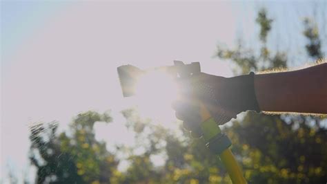 햇빛에 녹색 잔디밭에 물을 뿌리는 스프링클러가있는 정원 호스가있는 남자의 손 호스에서 물이 흐릅니다 반짝이는 물방울 남성 손 급수 정원 정원사 작업 원예 개념 30 34세에