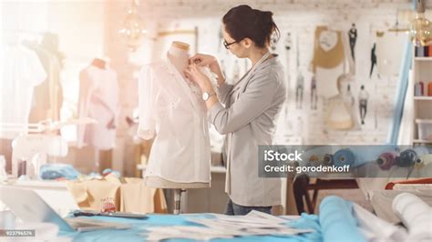 아름 다운 여자 패션 디자이너 맞게 마네킹 블라우스 조정 작업 그녀의 스튜디오는 밝은 써니 주위에 서 있는 마네킹 옷에 매달려 다채로운 직물 테이블에 누워 4k해상도에 대한