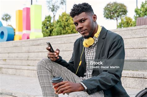 야외에서 블레이저를 착용하고 테이크 아웃 커피 컵을 들고 휴대 전화를 사용하는 쾌활한 젊은 아프리카 남자 20 29세에 대한 스톡 사진 및 기타 이미지 Istock