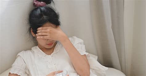 아픈 여자는 침실의 침대에 누워있는 동안 물 한 잔을 들고 알약을 먹습니다 사진 Unsplash의 두통 이미지