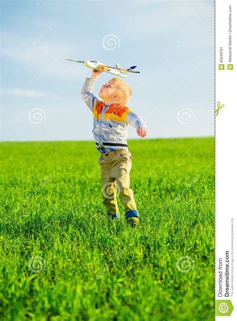 Счастливый мальчик играя с самолетом игрушки против голубого неба лета ...