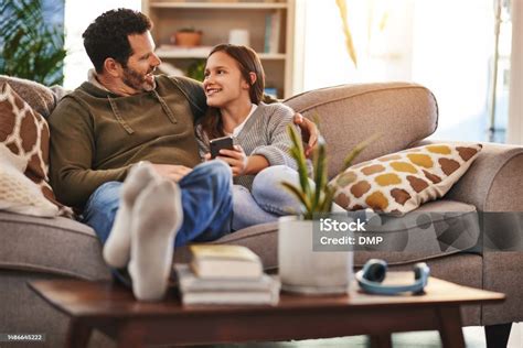 전화 행복한 남자와 십대 소녀는 소파에서 소셜 미디어 밈을 확인하고 집에서 휴식을 취할 수 있는 좋은 시간을 보냅니다 라운지 소파에 앉은 아빠와 딸 인터넷 게시물 함께 웃고